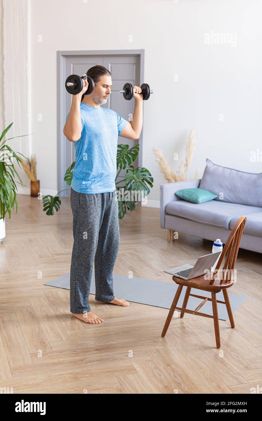 Vertical photo of a middle-aged man works out at home with dumbbells in ...