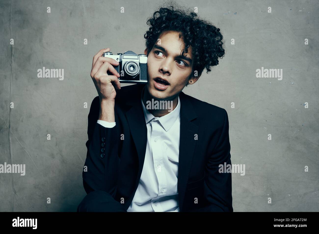 curly-haired man in a jacket and shirt holding a camera in his hand ...