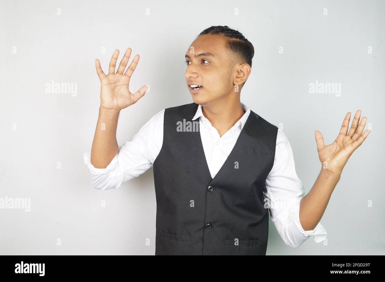 A young shocked Indian man in waistcoat vest with hands raised up ...