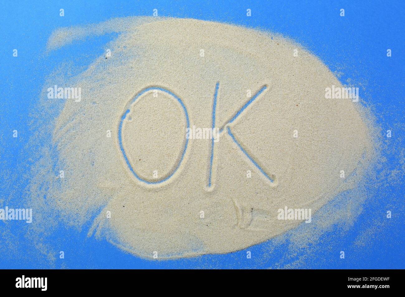 The word ok is written in the sand on a blue background Stock Photo - Alamy