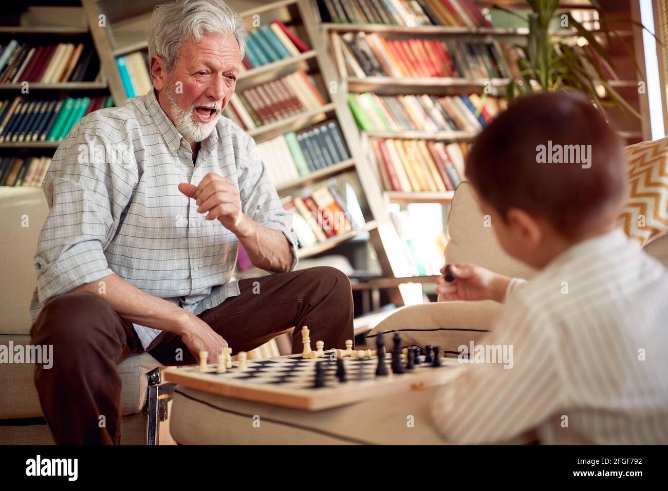 A cheerful Grandpa enjoys playing the chess with his little grandson ...