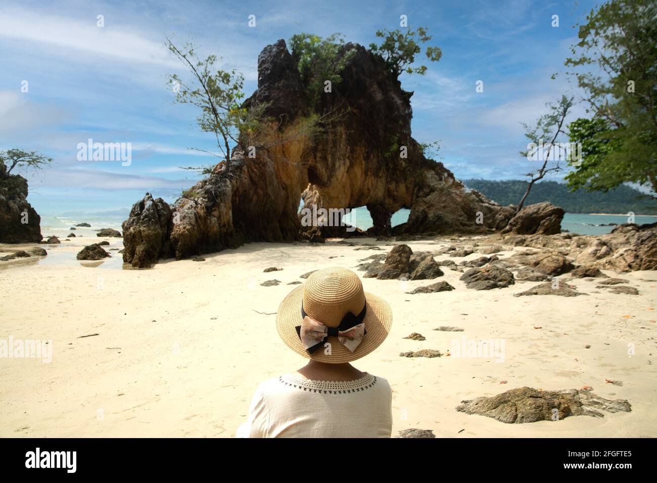 Asian female tourists sit on the rocks at the beach and look at the ...