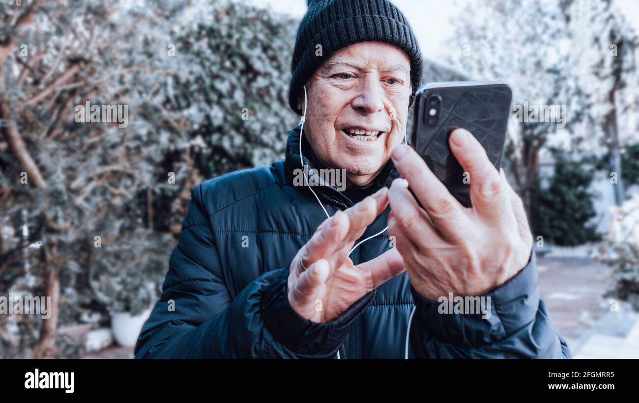 Smiling older man makes a video call with his black smart phone and ...
