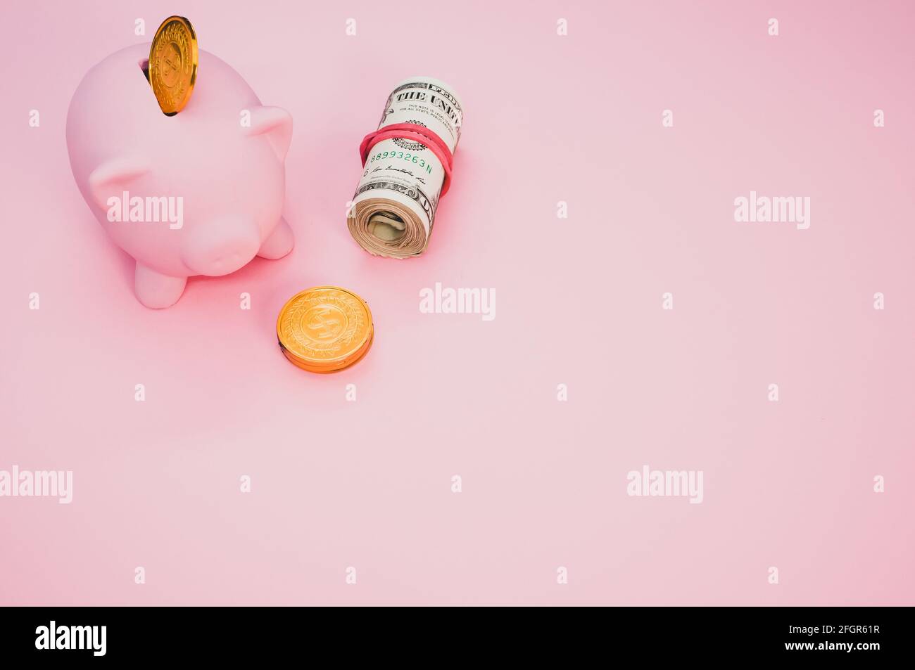 A closeup of a piggy bank with coins next to a roll of dollars isolated ...