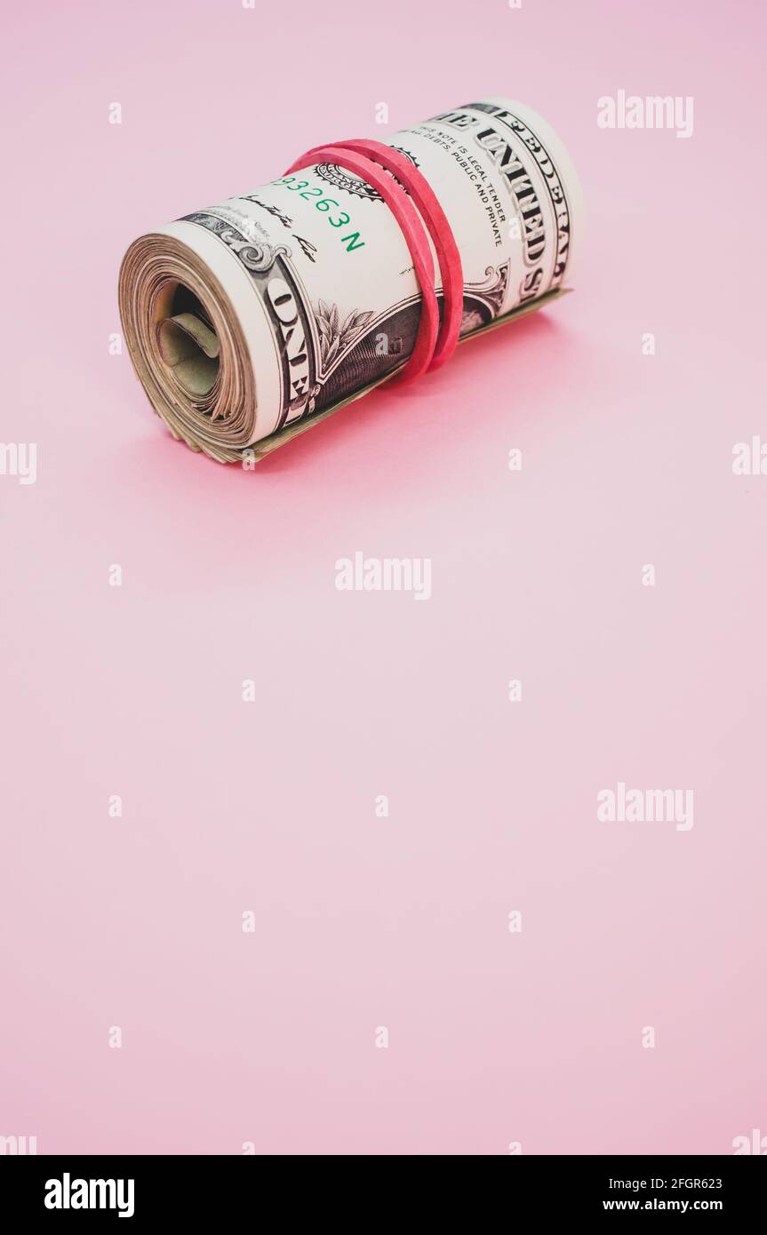 A vertical shot of a roll of dollars isolated on pink background for a ...