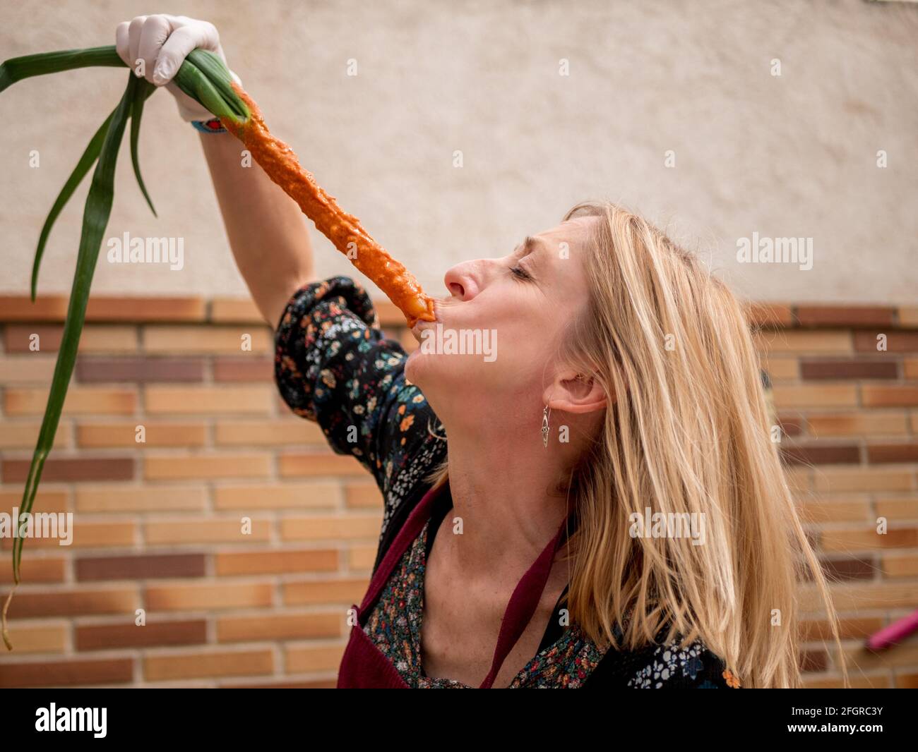 A blonde female eating barbecue of spring onion shoots with tomato ...