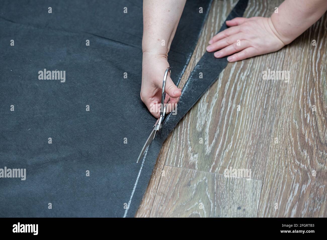 Woman's hand cuts black covering material on the floor in the house ...
