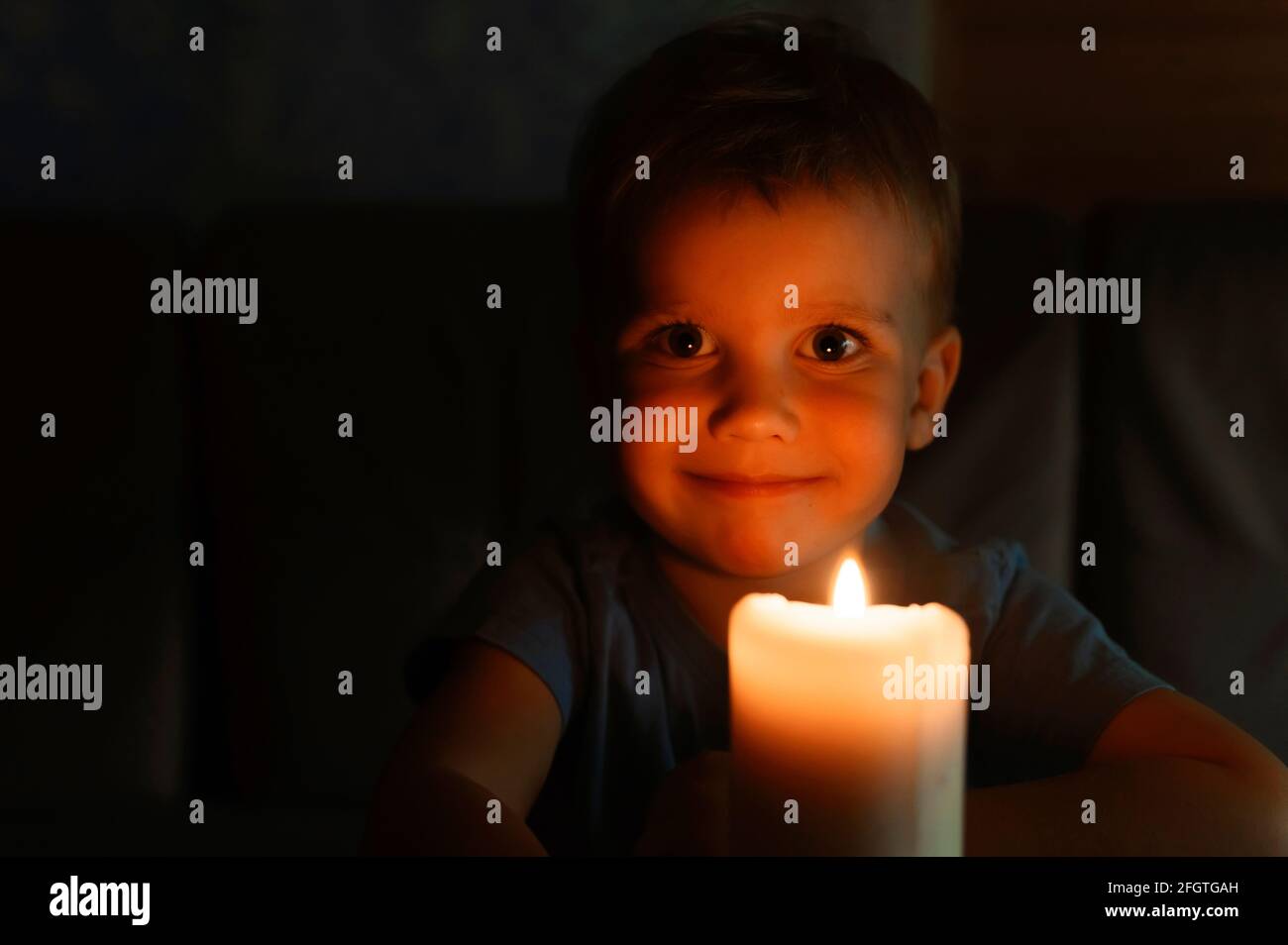 little kid boy of four years old admires a burning wax candle in the ...