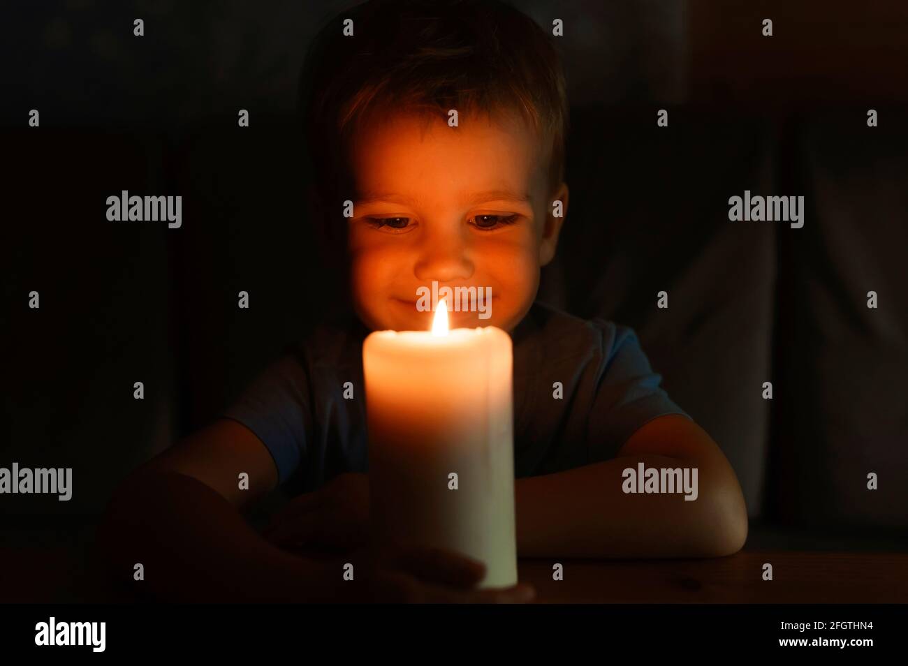 little kid boy of four years old admires a burning wax candle in the ...