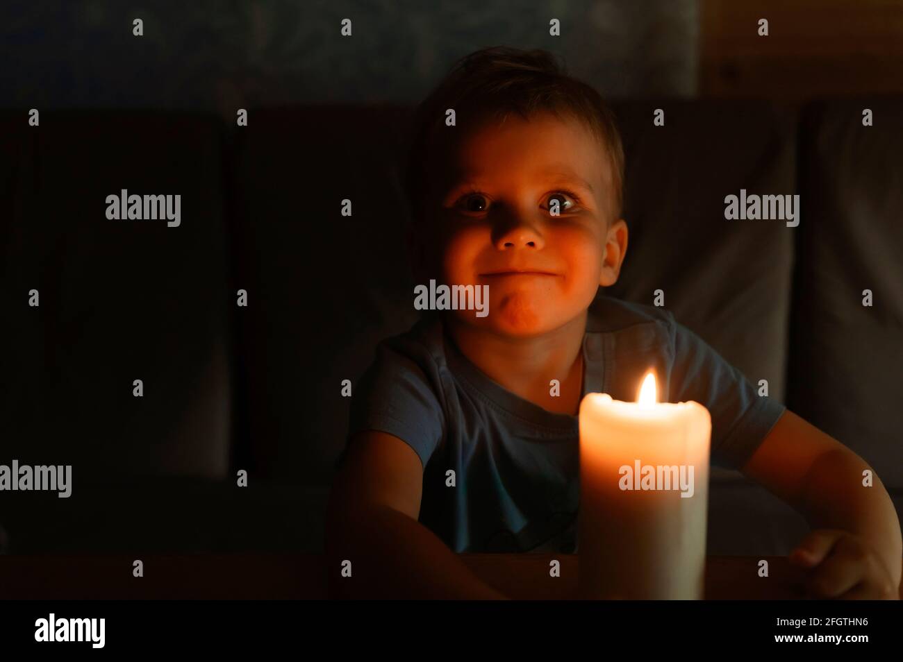 little kid boy of four years old admires a burning wax candle in the ...