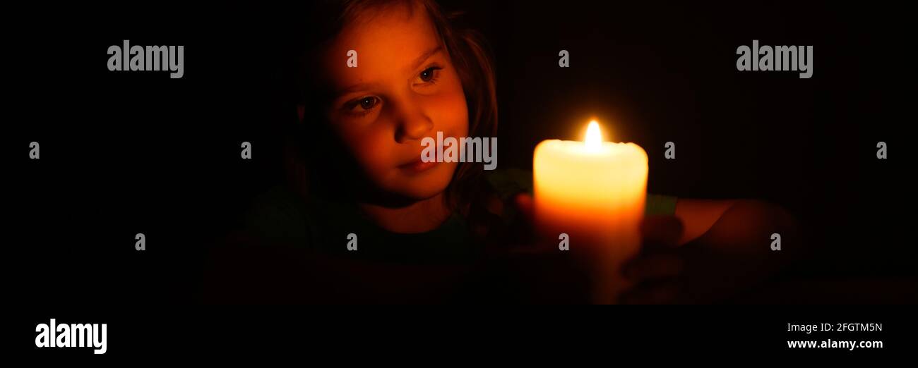 kid girl of seven years old admires a burning wax candle in the evening ...