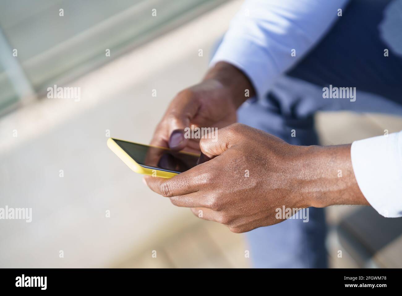 Hands of unrecognizable black man using a smartphone sitting on a urban ...