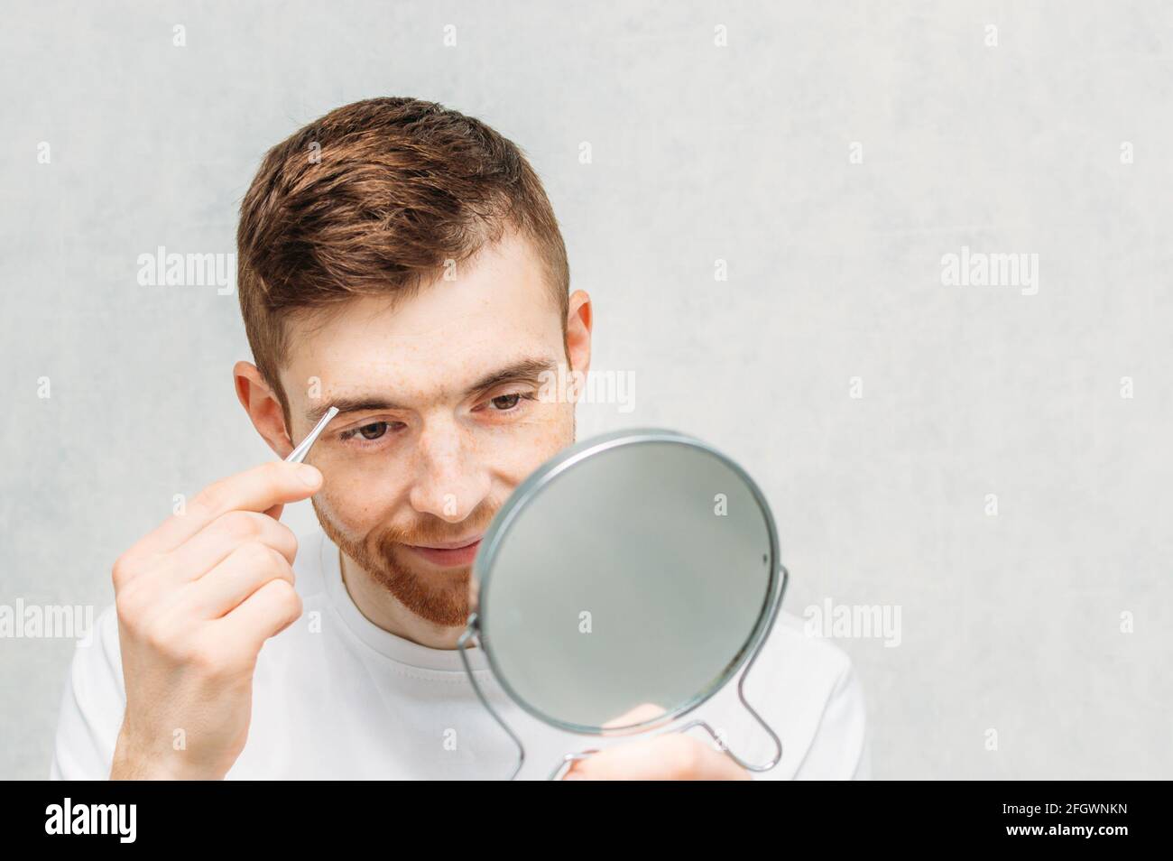 young guy with a smile on his face plucks his eyebrows Stock Photo - Alamy