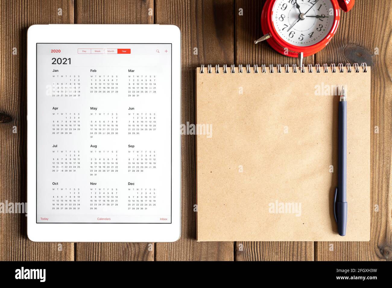 a tablet with an open calendar for 2021 year, a red alarm clock, and a ...