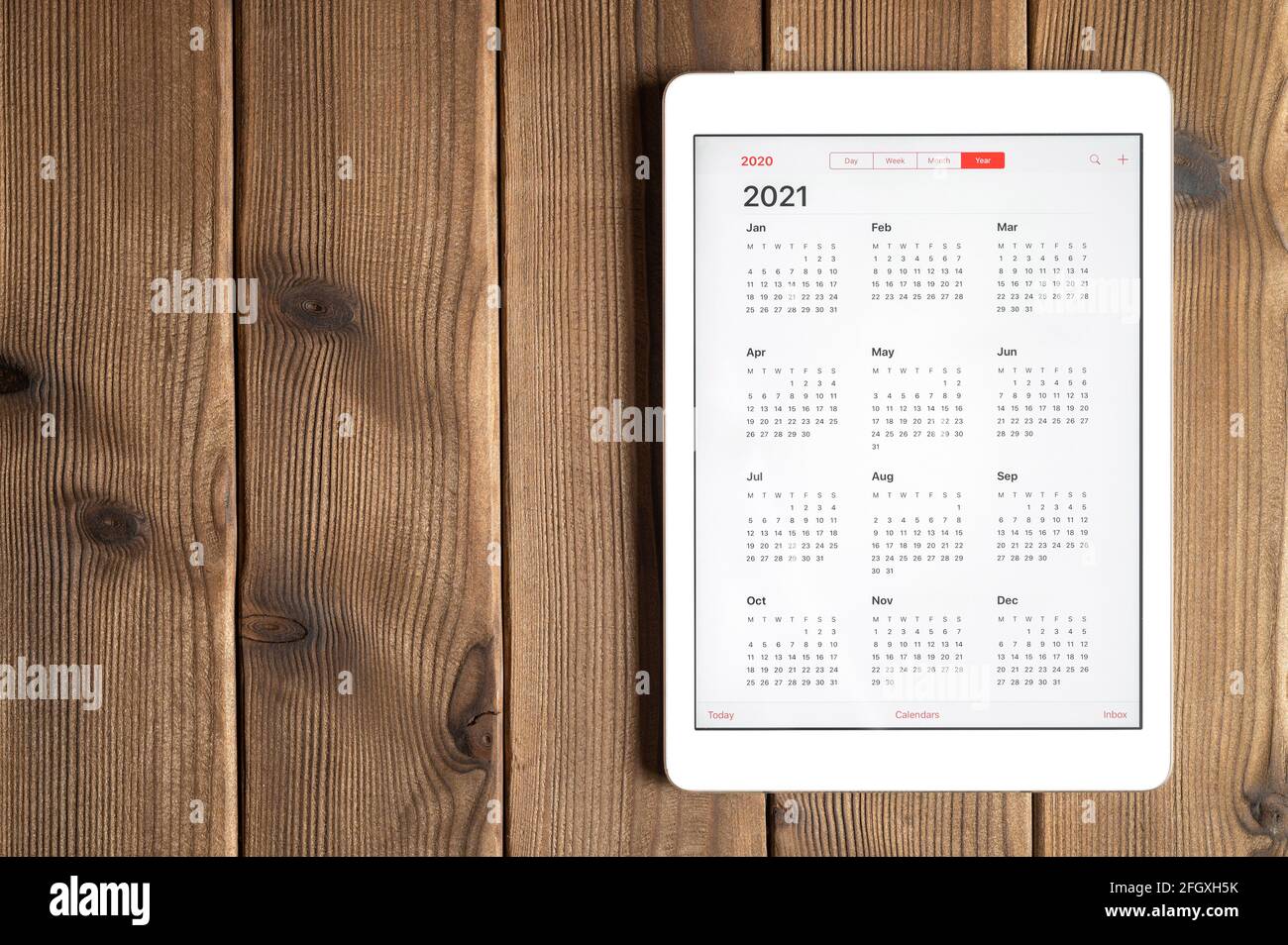 a tablet with an open calendar for 2021 year on a wooden boards table ...