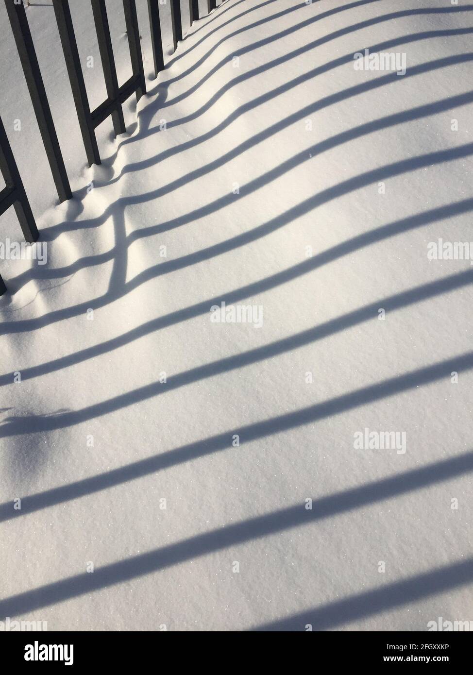 a fence and the shadow of the fence on the snow on a sunny day ...