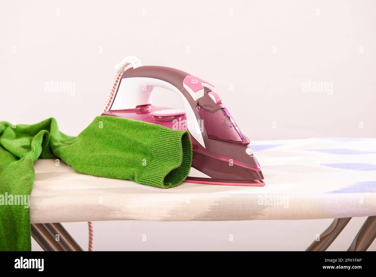 Steam iron and ironing clothes green sweater on ironing board isolated ...