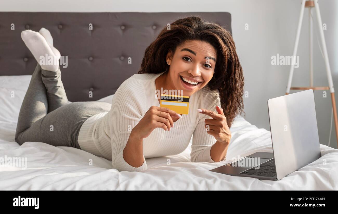 Happy black woman showing debit credit card, using laptop Stock Photo ...