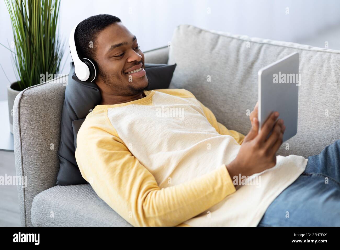 Joyful black guy laying on couch, watching movies on pad Stock Photo ...