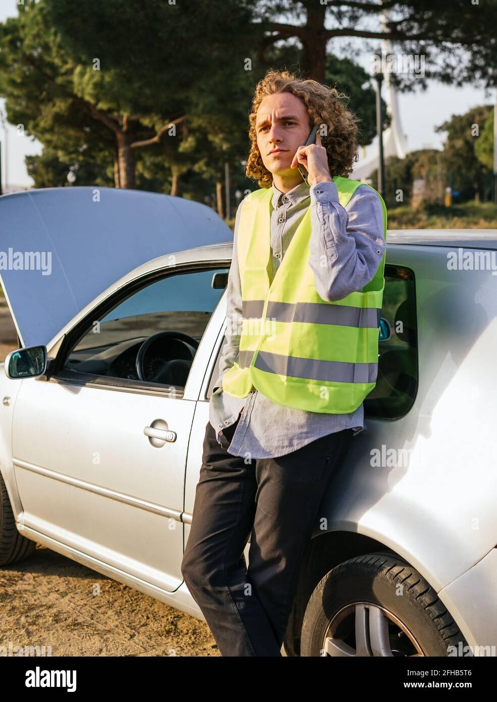 Side view of male driver in safety vest standing near auto with open ...