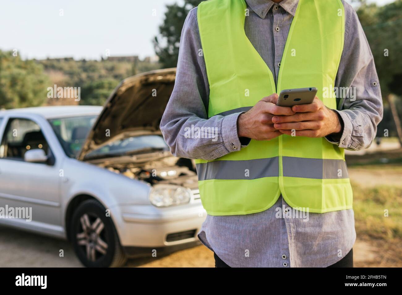 Crop unrecognizable male driver in green safety vest using mobile phone ...