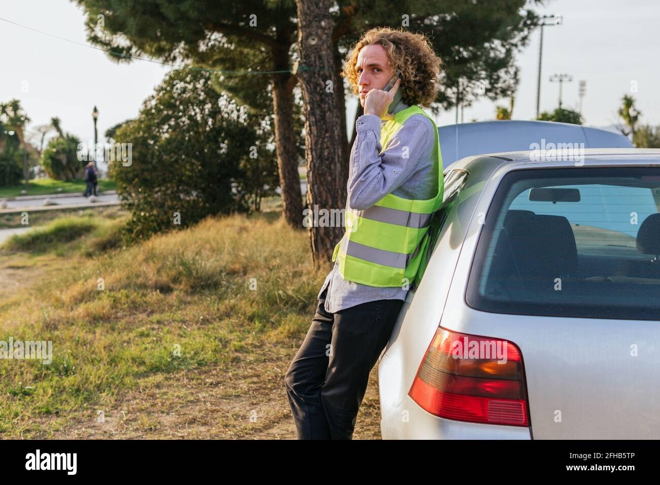 Side view of male driver in safety vest standing near auto with open ...