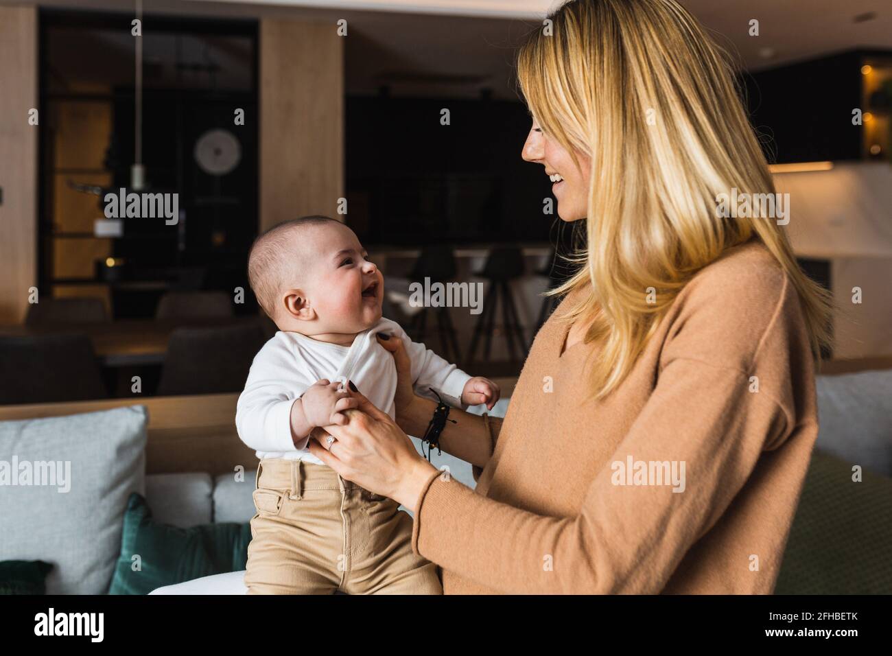 Side view of delighted mother holding adorable smiling baby while ...