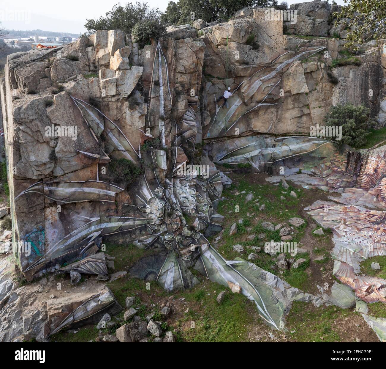 Drone view of man in helmet hanging on rope while painting graffiti on ...