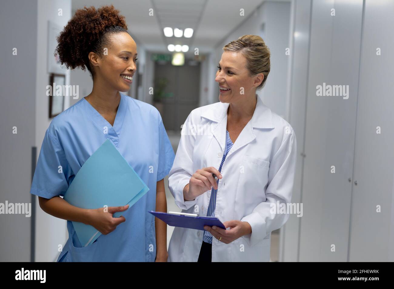 Two diverse female doctors standing in hospital corridor smiling to ...