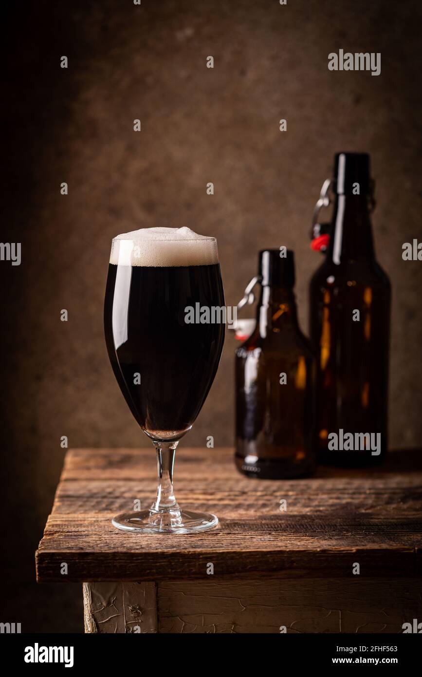 Glass of dark beer with foam head on dark wooden background with empty ...