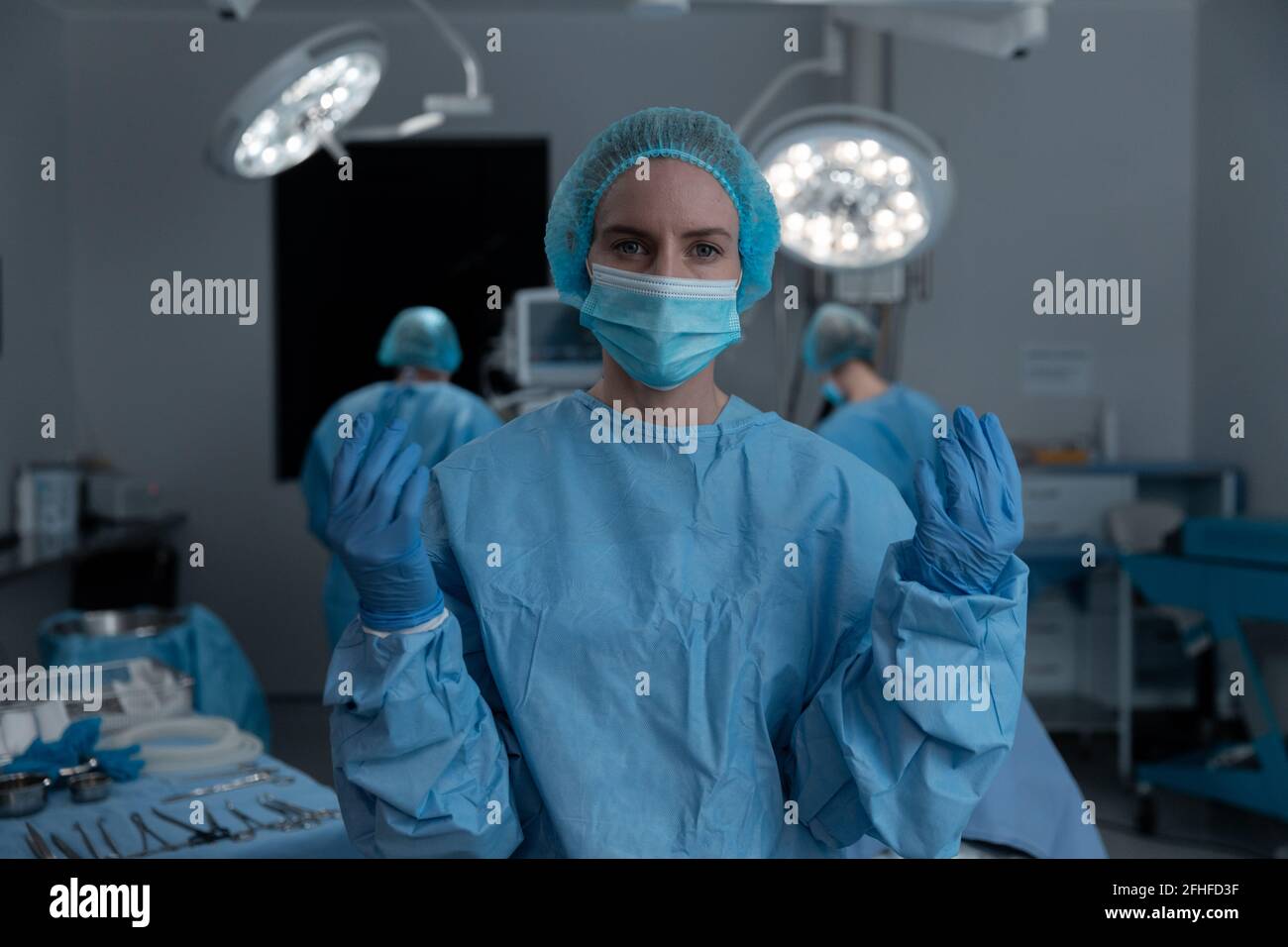 Portrait of caucasian female surgeon wearing face mask, gloves, cap and ...
