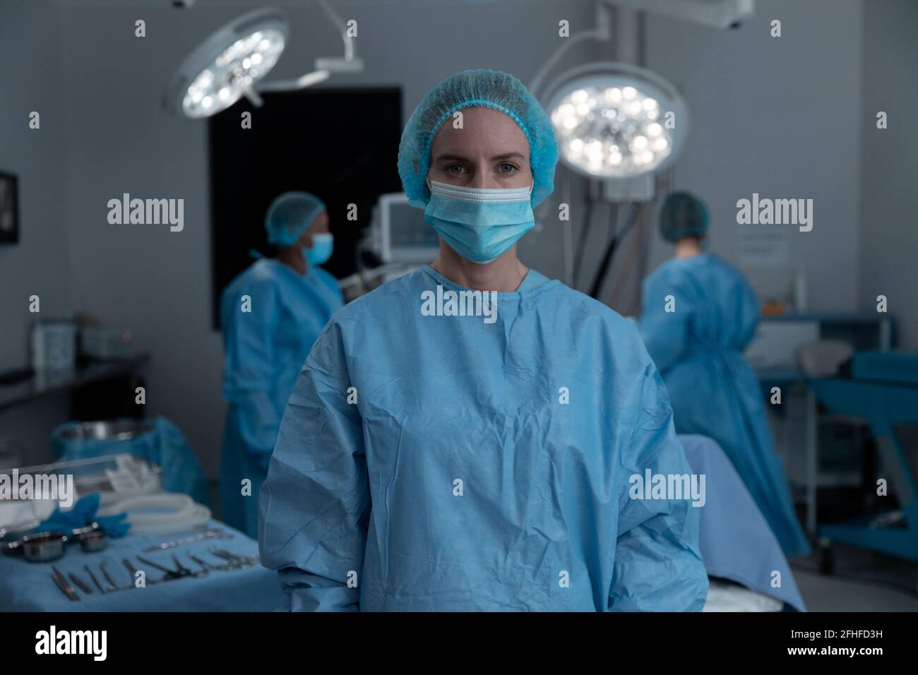 Portrait of caucasian female surgeon wearing face mask, surgical cap ...
