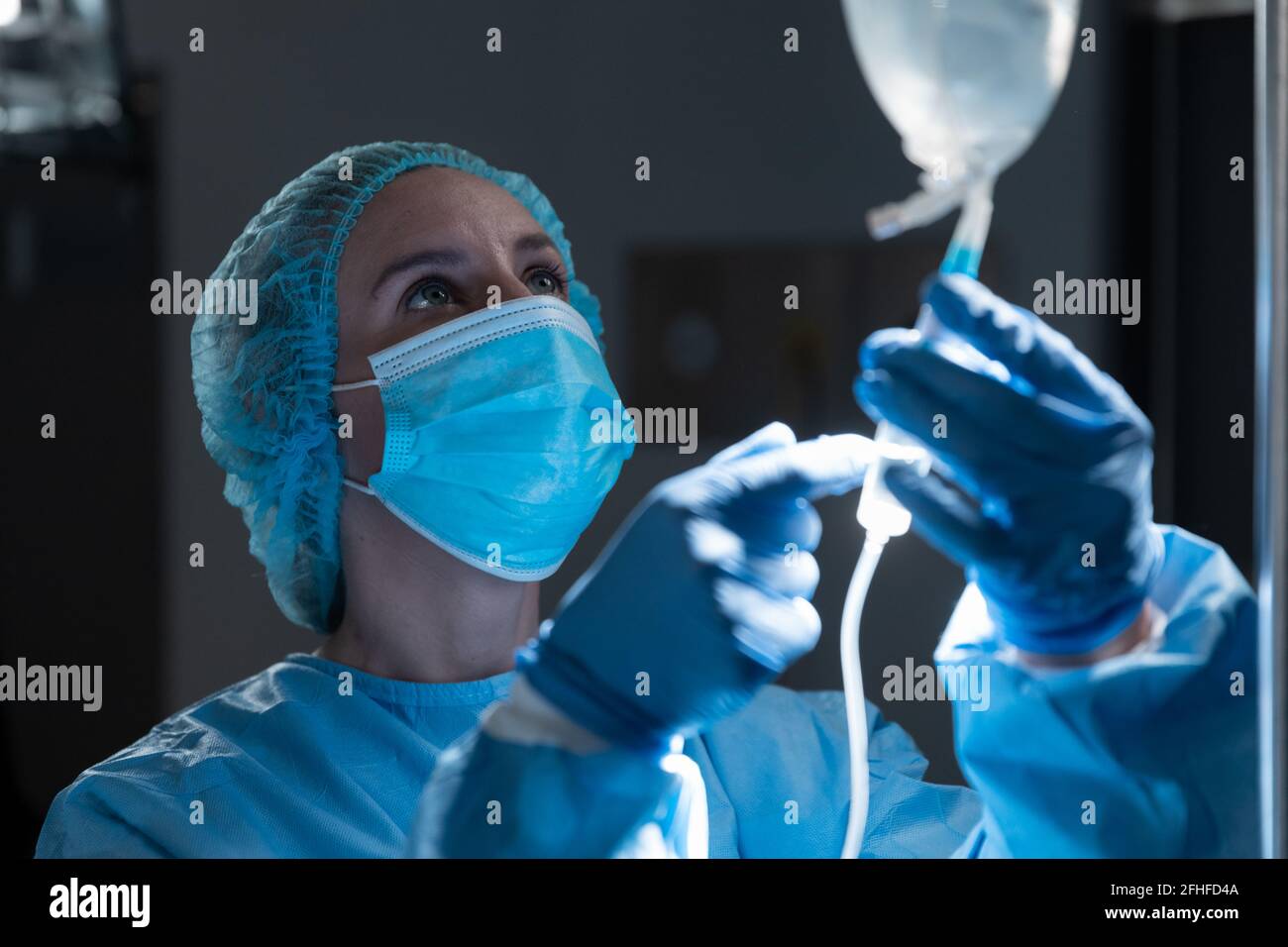 Caucasian female doctor wearing face mask preparing iv drip bag for ...