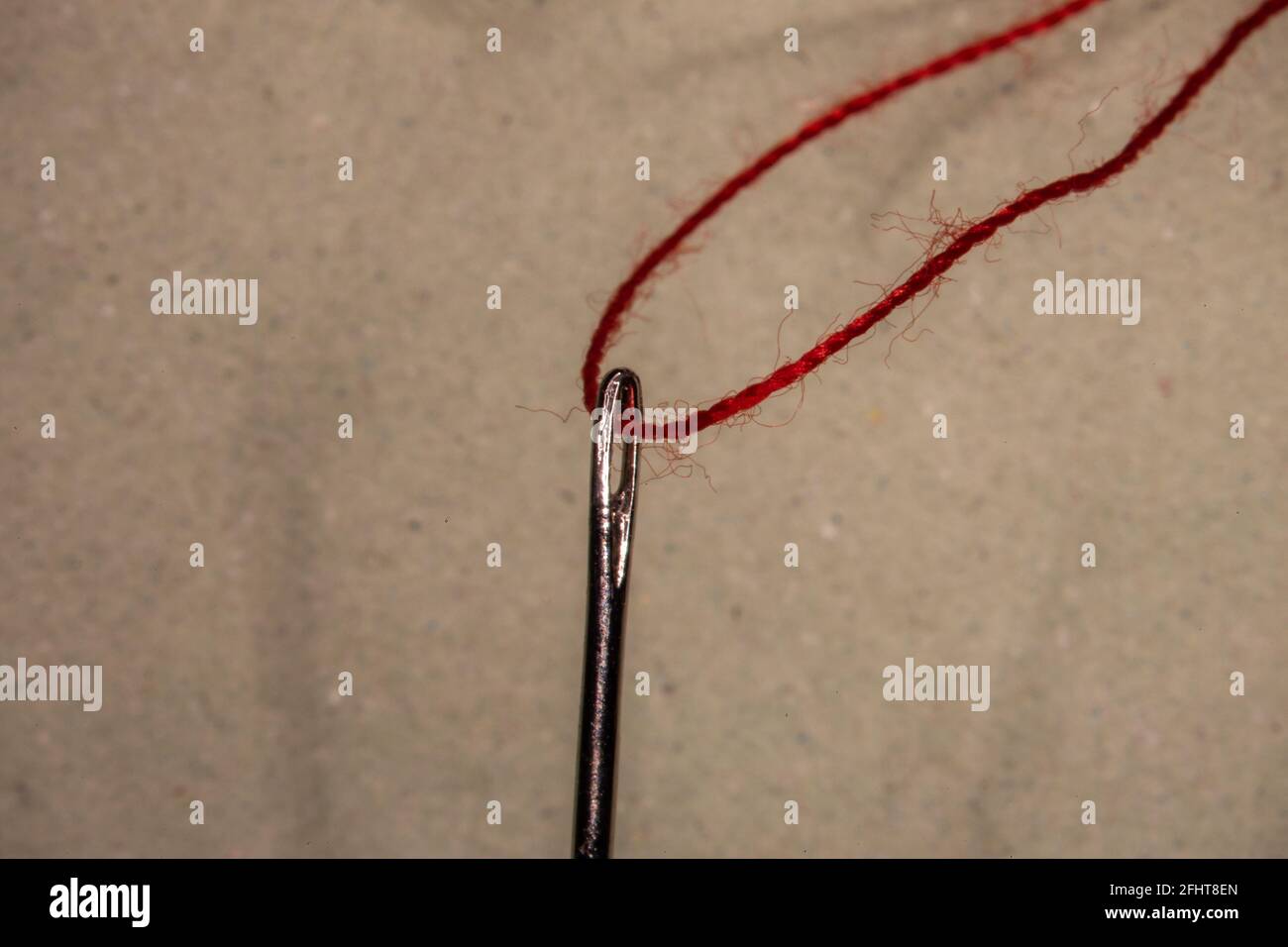 a red thread is threaded into a sewing needle Stock Photo - Alamy