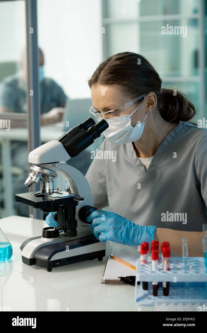 Concentrated female virologist in protective goggles and latex gloves ...