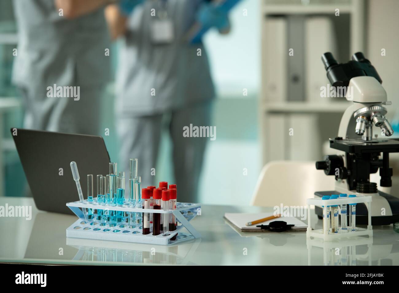 Desk of laboratory researcher: test tube racks, clipboard, laptop and ...