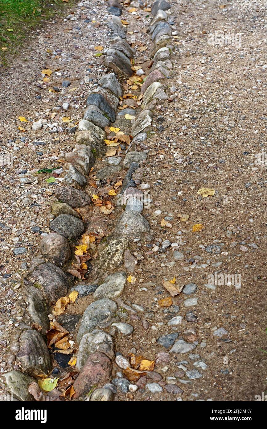 Drainage ditch laid out of stones on a pedestrian path in the park of ...