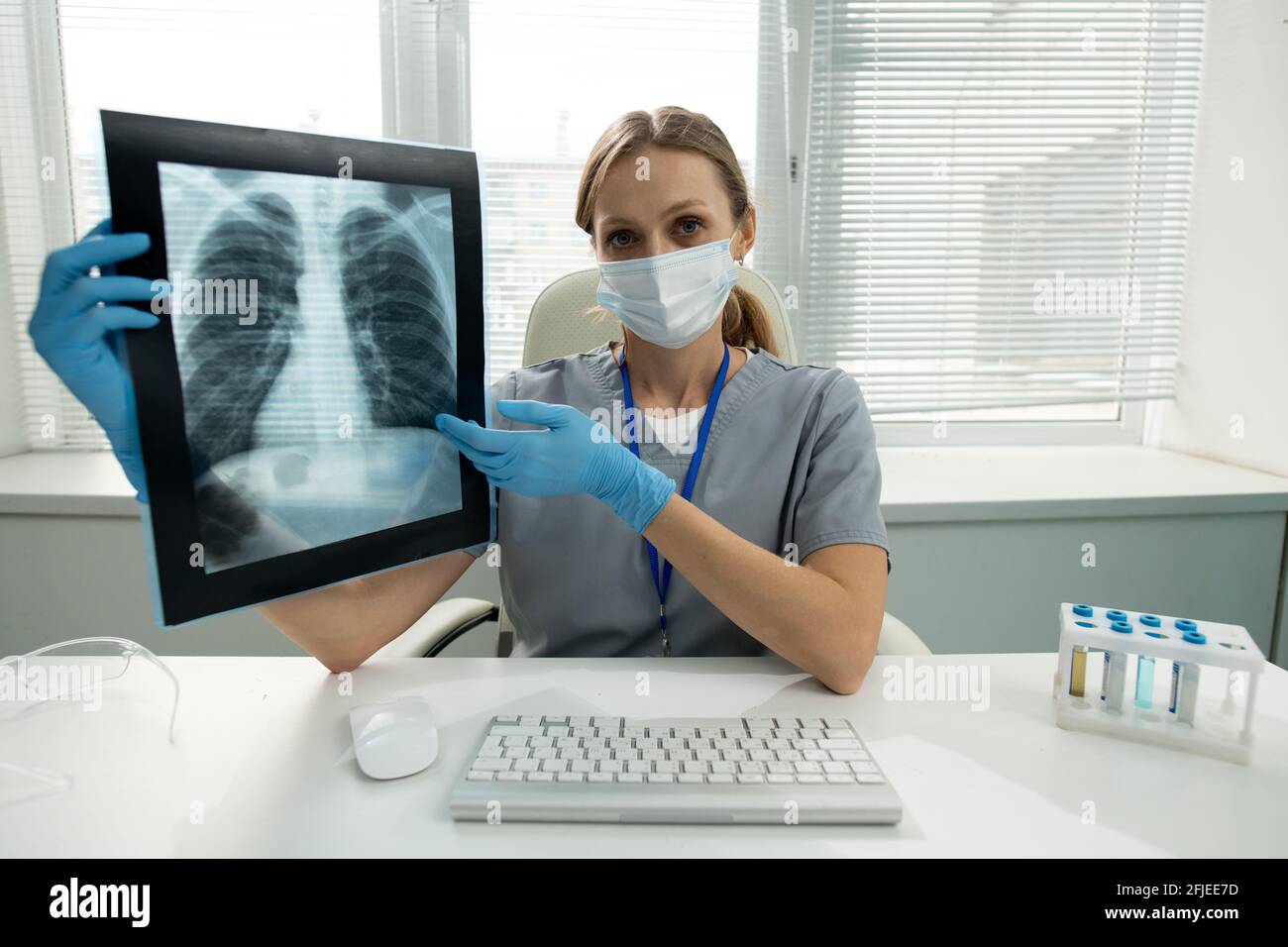 Portrait of female radiologist in mask and gloves sitting at desk with ...