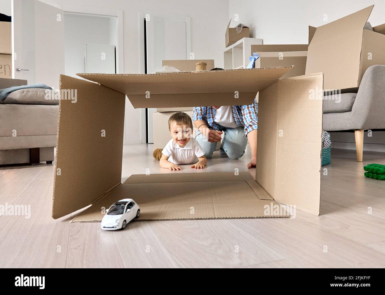 Happy kid son playing toy car with dad unpacking boxes on moving day ...