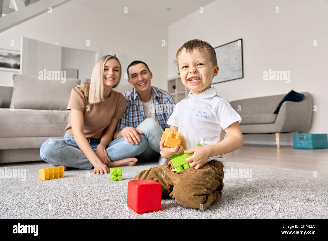 Cute happy kid toddler son playing toys with young parents at home ...