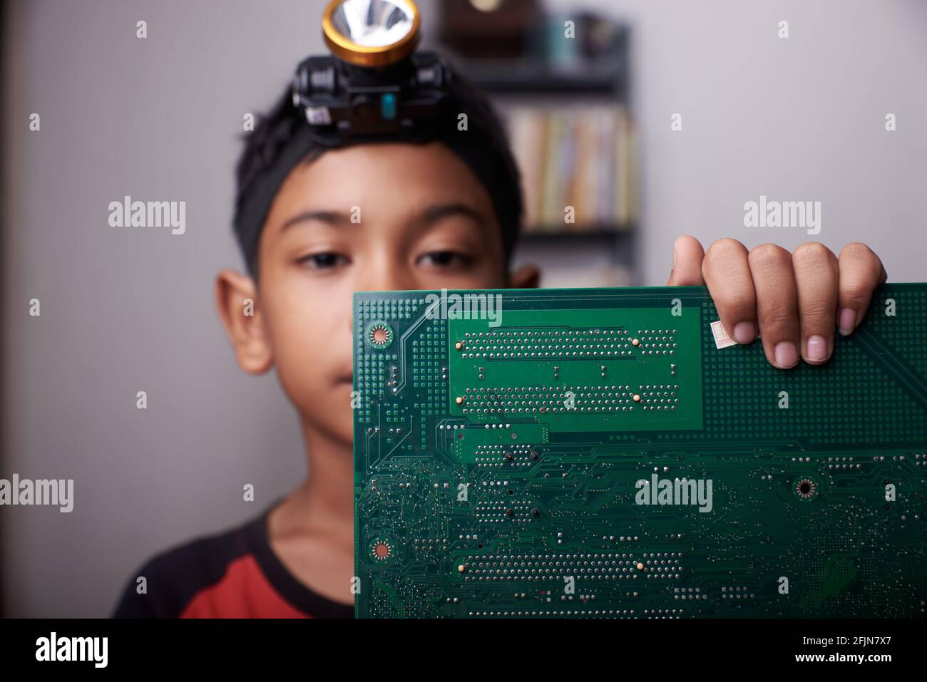 Little boy holding the motherboard, studying computer component at home ...