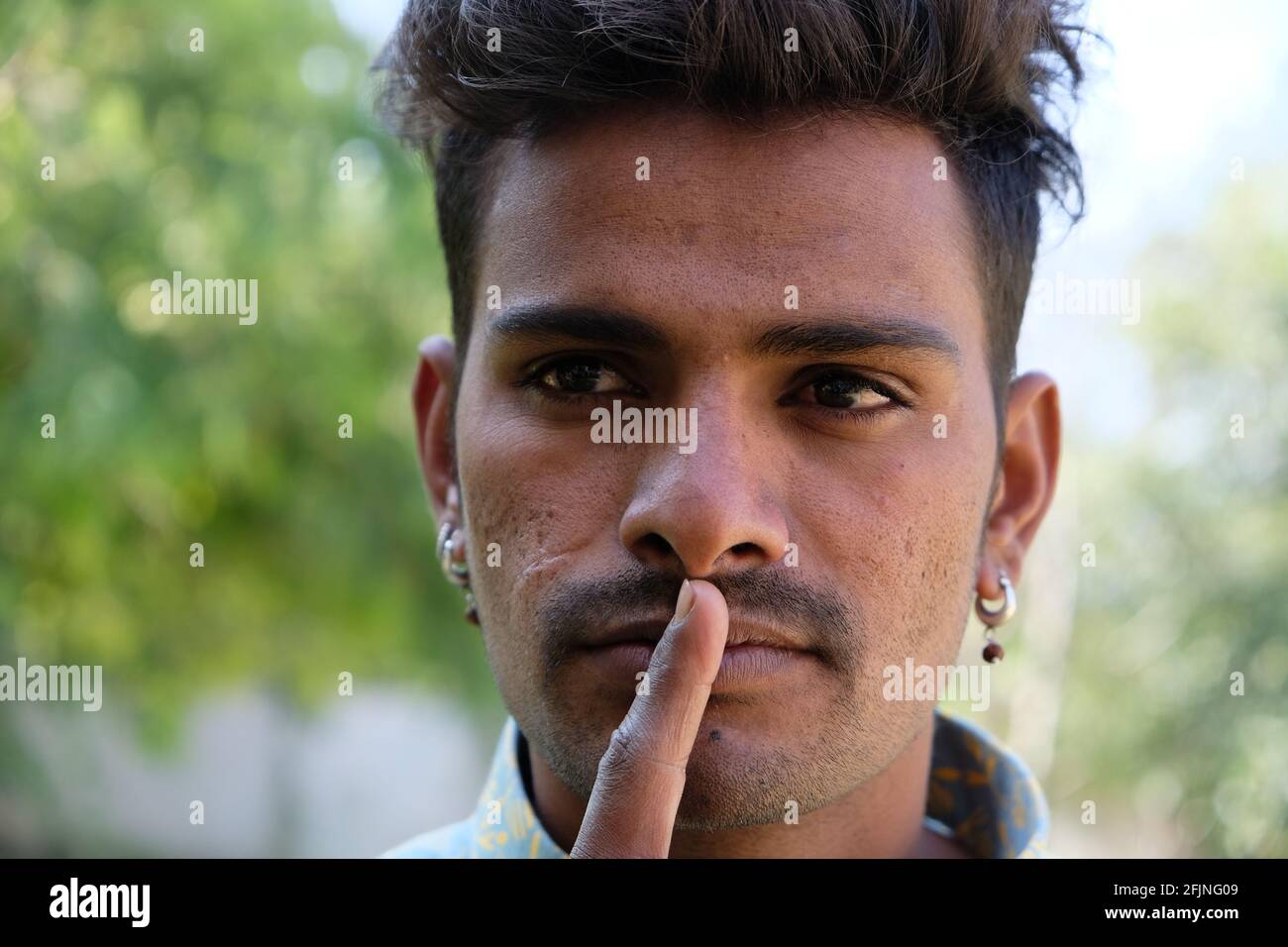 A portrait of a young handsome Indian male holding index finger on lips ...