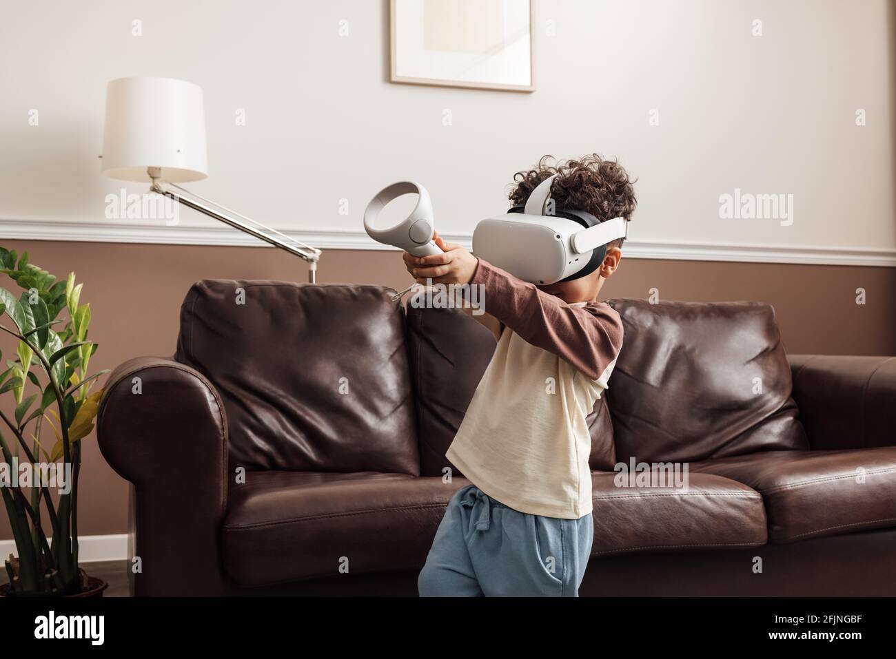 Kid playing virtual reality game in a living room holding joystick with ...