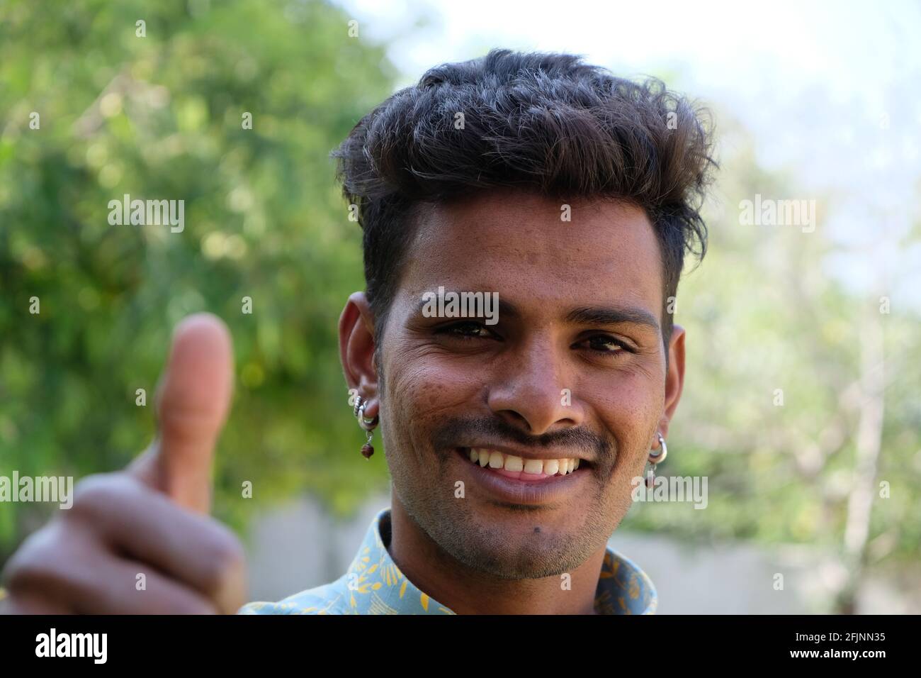 A portrait of a happy smiling Indian male standing in a park showing ...