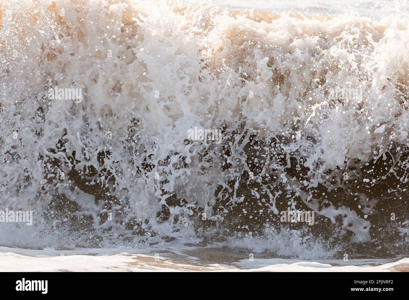 Closeup of a wave breaking on a beach. The wave is filled with bubbles ...