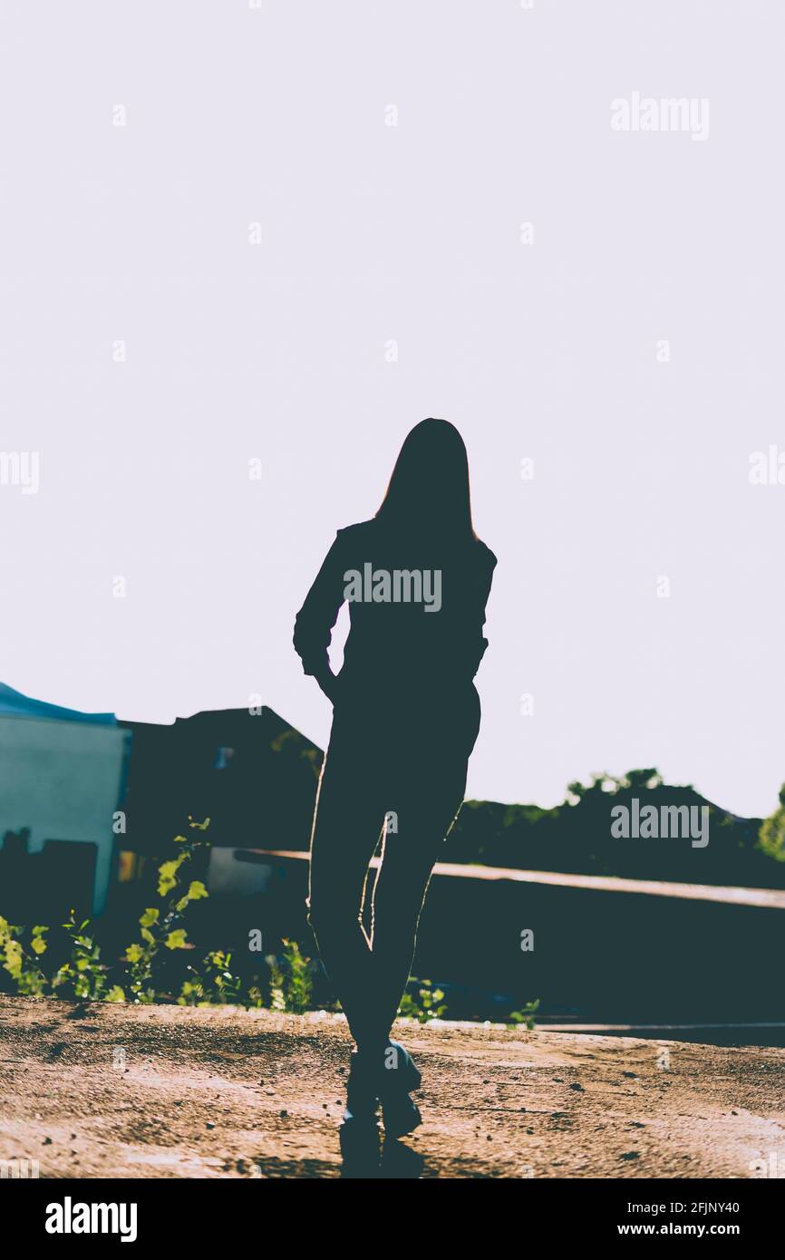 A silhouette of a young woman standing outside with the sun shining ...