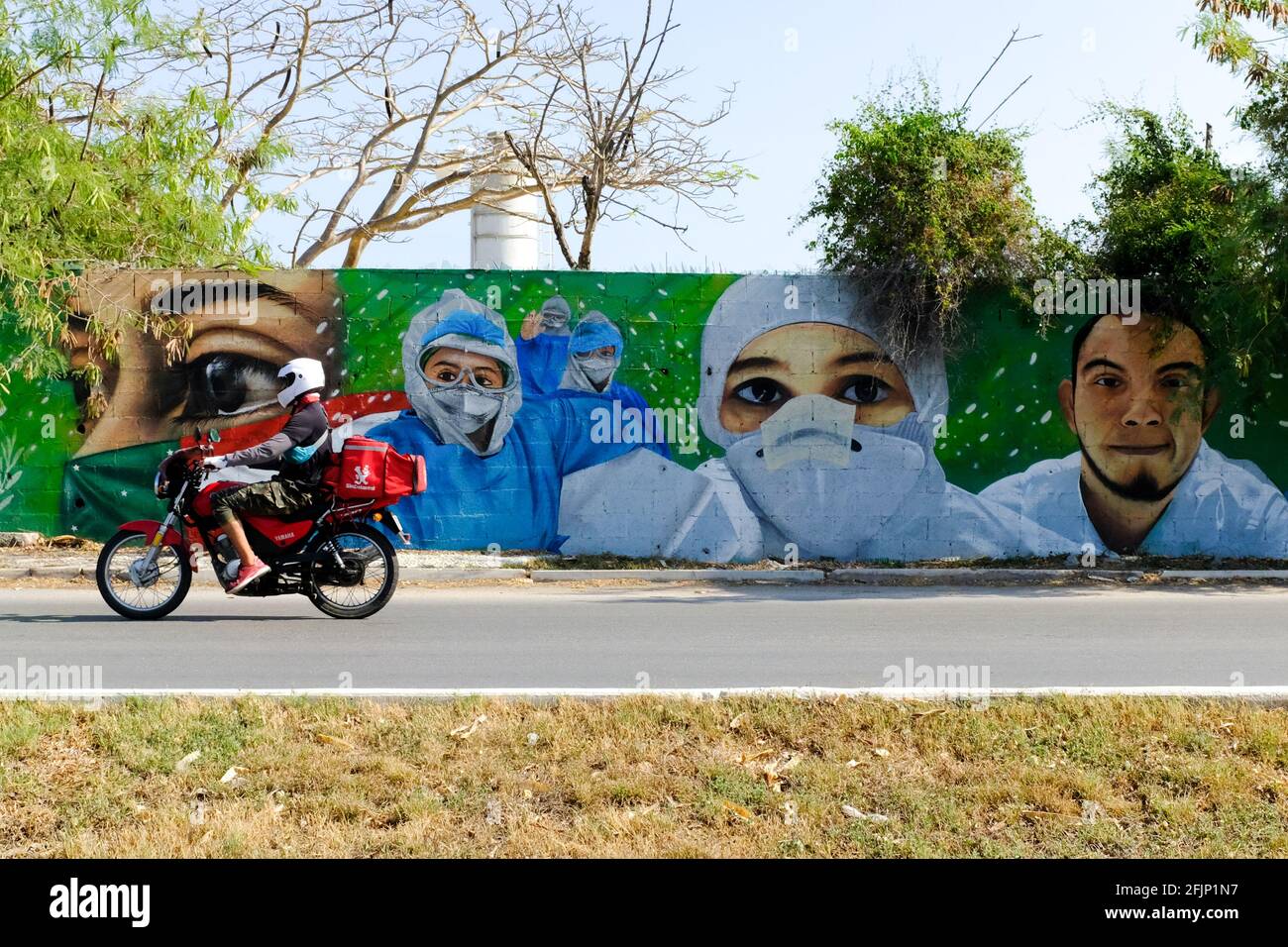 Motorcycle passing in front of a mural portraying the Covid-19 first ...