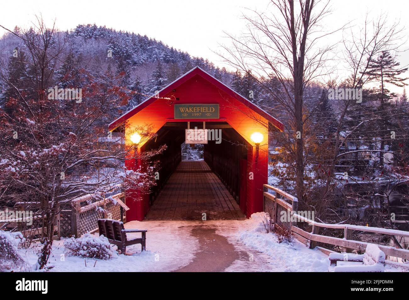 Red Covered Bridge in winter with snow-covered trees on the hillside ...