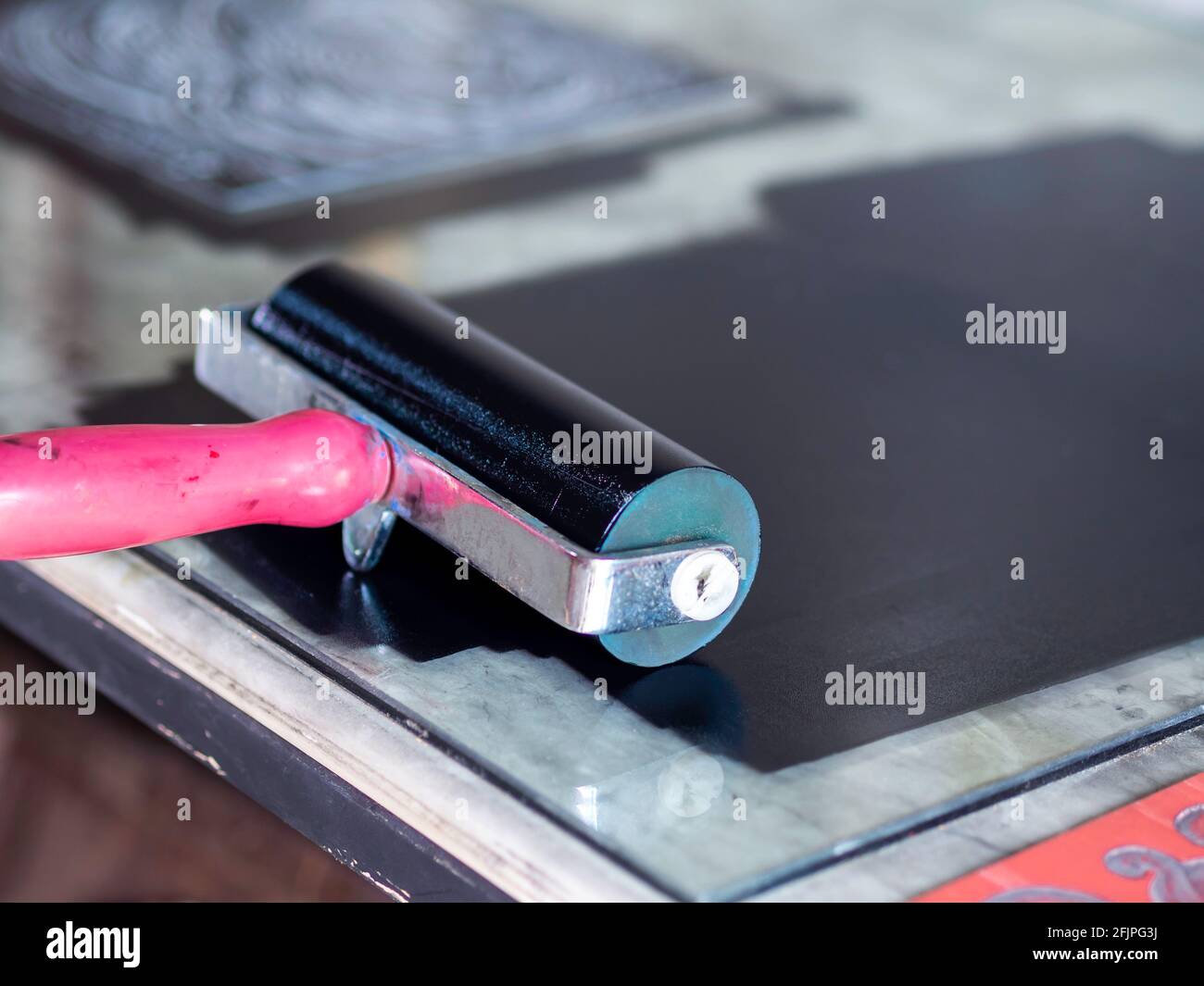 Close-up printmaking roller with red handle on black relief ink color ...