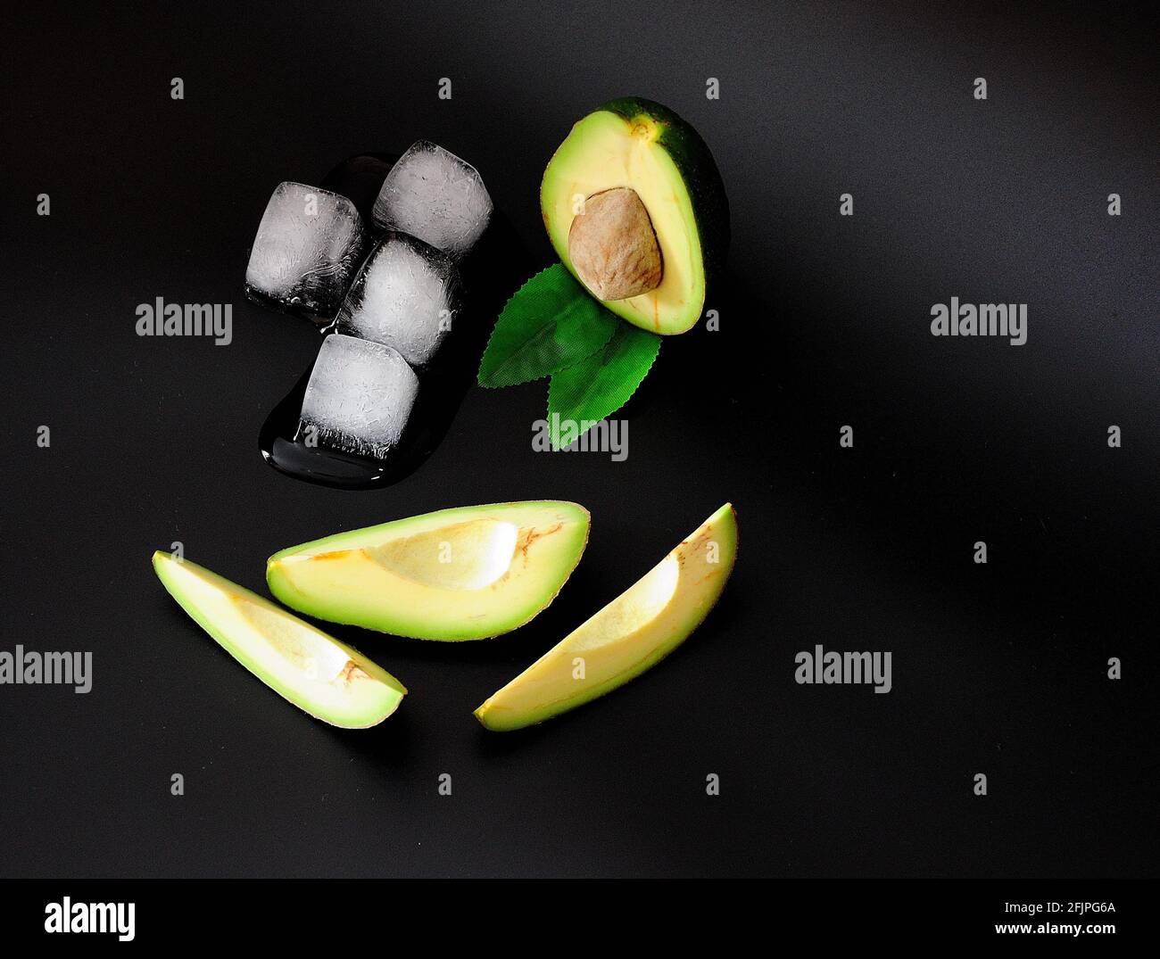 Pieces of ripe sliced avocado and cubes of melted ice on a black ...